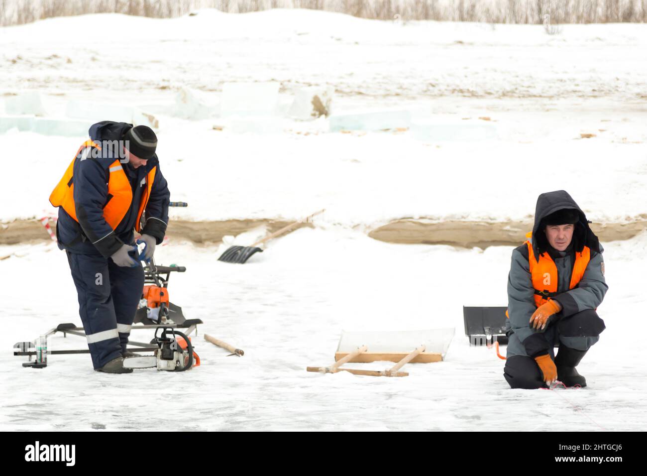 Workers fitters in orange life jackets on the ice of a frozen lake on ...