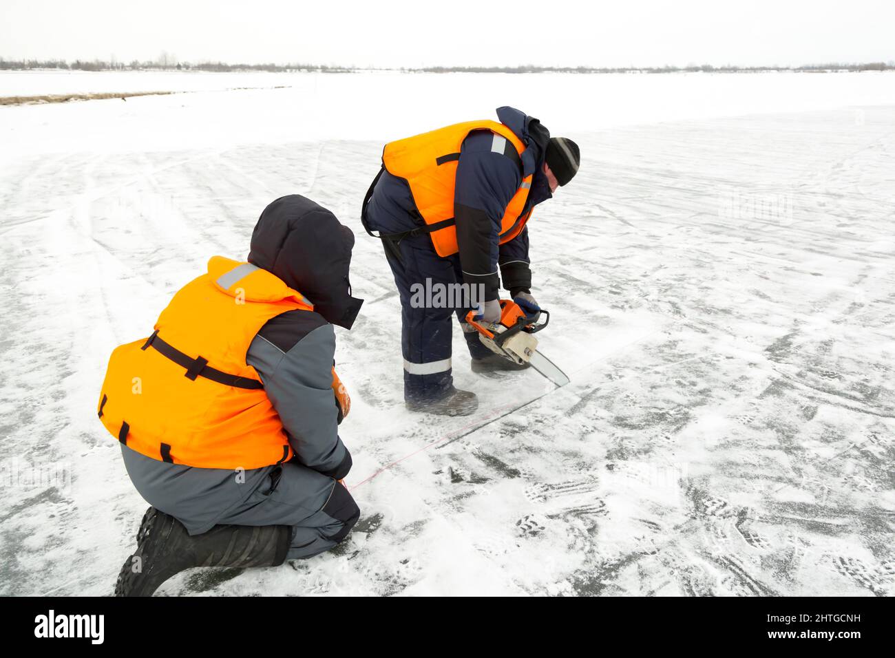 Workers fitters in orange life jackets on the ice of a frozen lake on ...