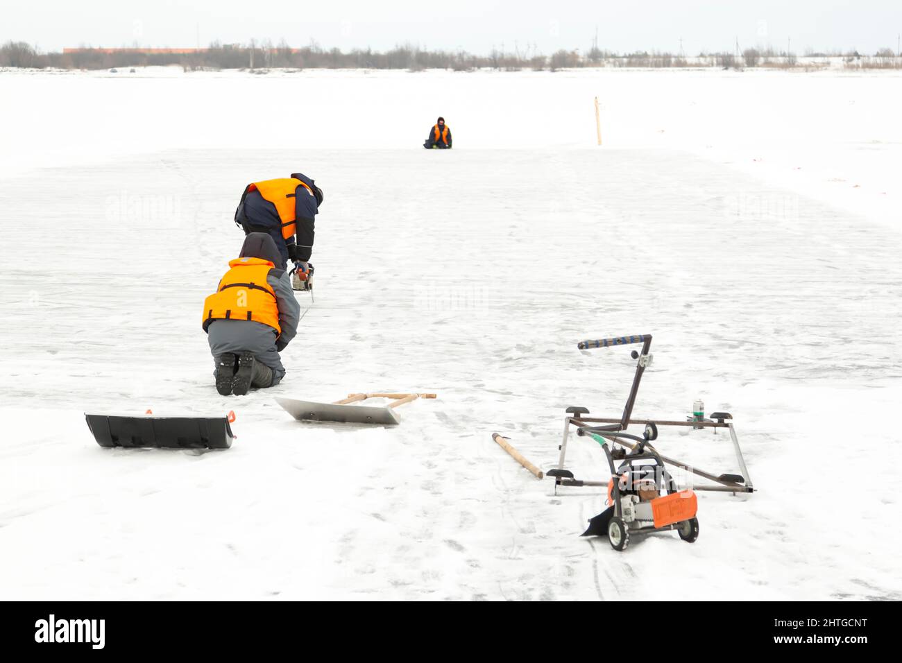 Workers fitters in orange life jackets on the ice of a frozen lake on ...
