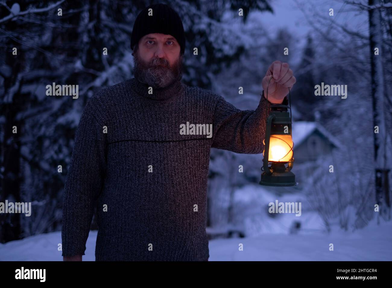 A man with a kerosene lamp in his hand walks through the snowy forest ...