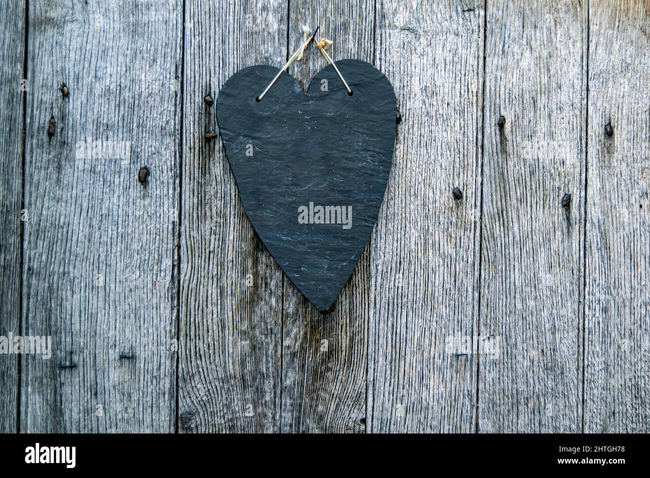 Plain black slate heart plate hung on a wooden surface with rusted ...