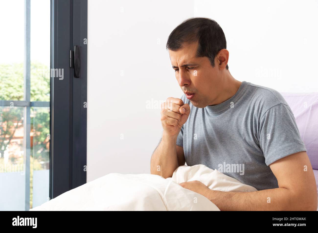 Shot of a handsome young man suffering with thecoughing as symptom for ...
