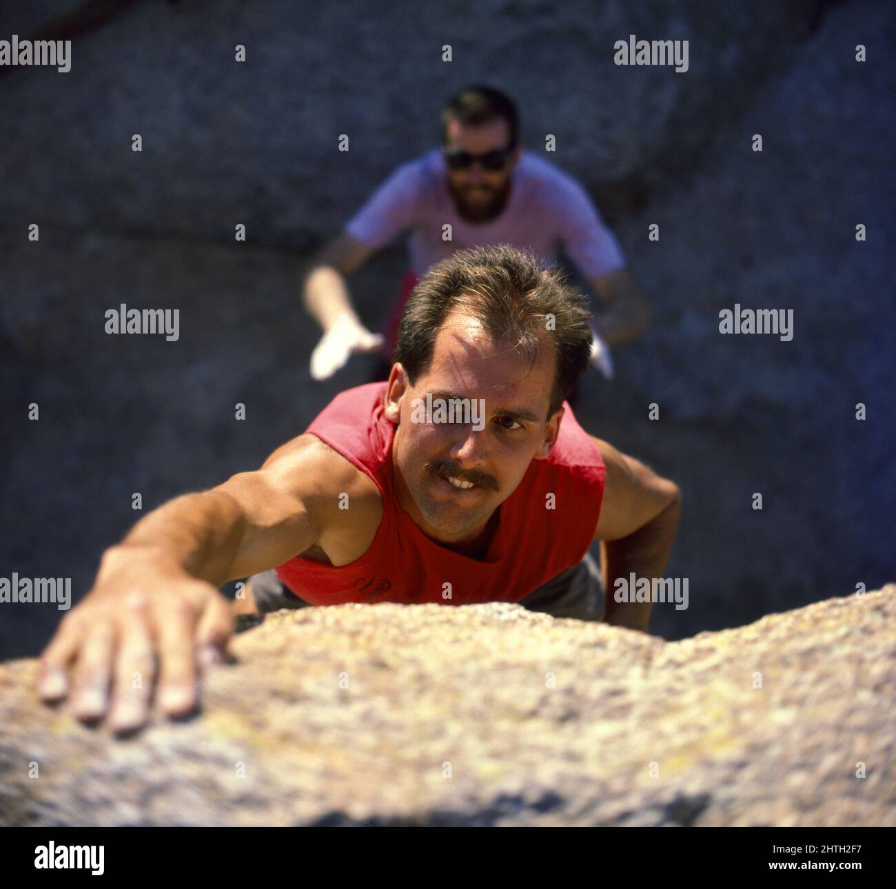 With the help of a spotter, a rock climber ascends a high boulder ...