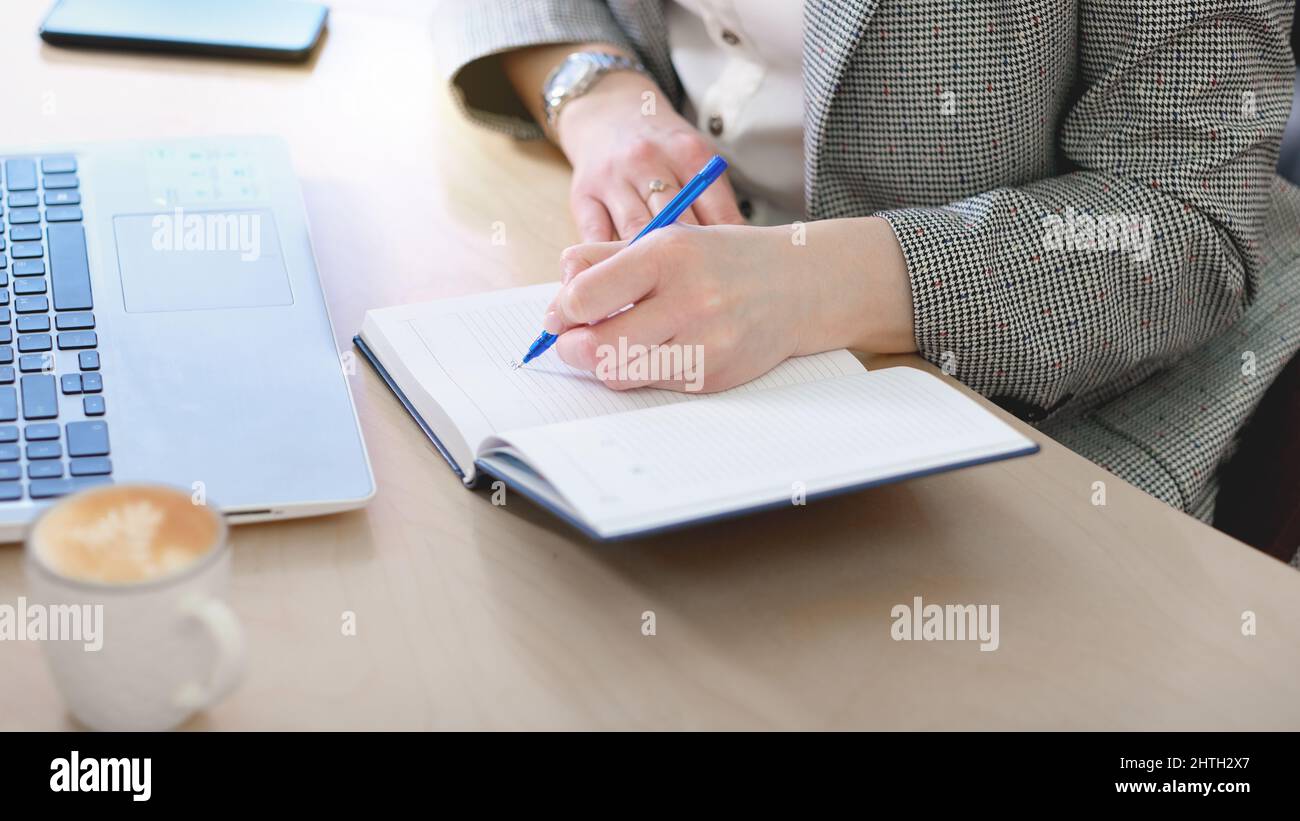 woman in formal clothes making notes in a diary. left handed person ...