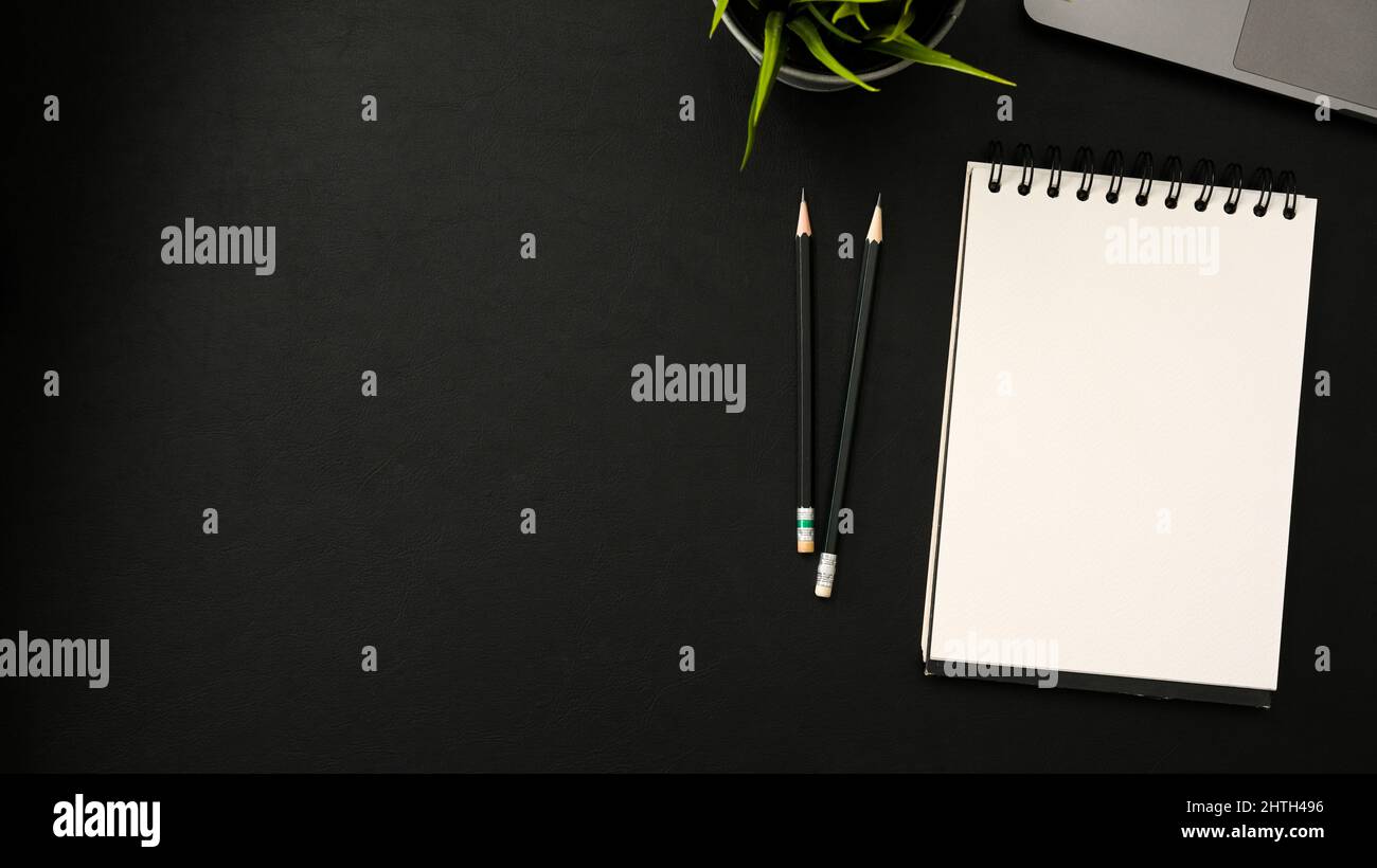 Black study table with empty spiral notepad, pencils, laptop, decor ...
