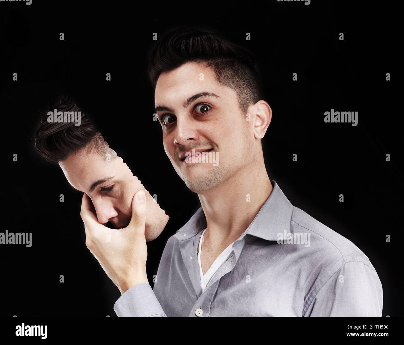 Lurking insanity. Young man lifting a mask off his face and revealing a ...