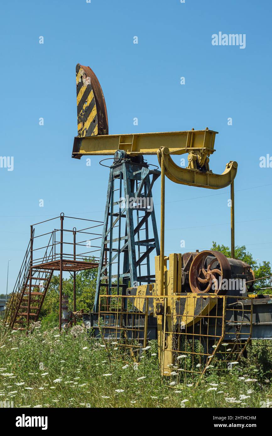 A yellow abandoned oil rig in a field against a blue sky. The concept ...