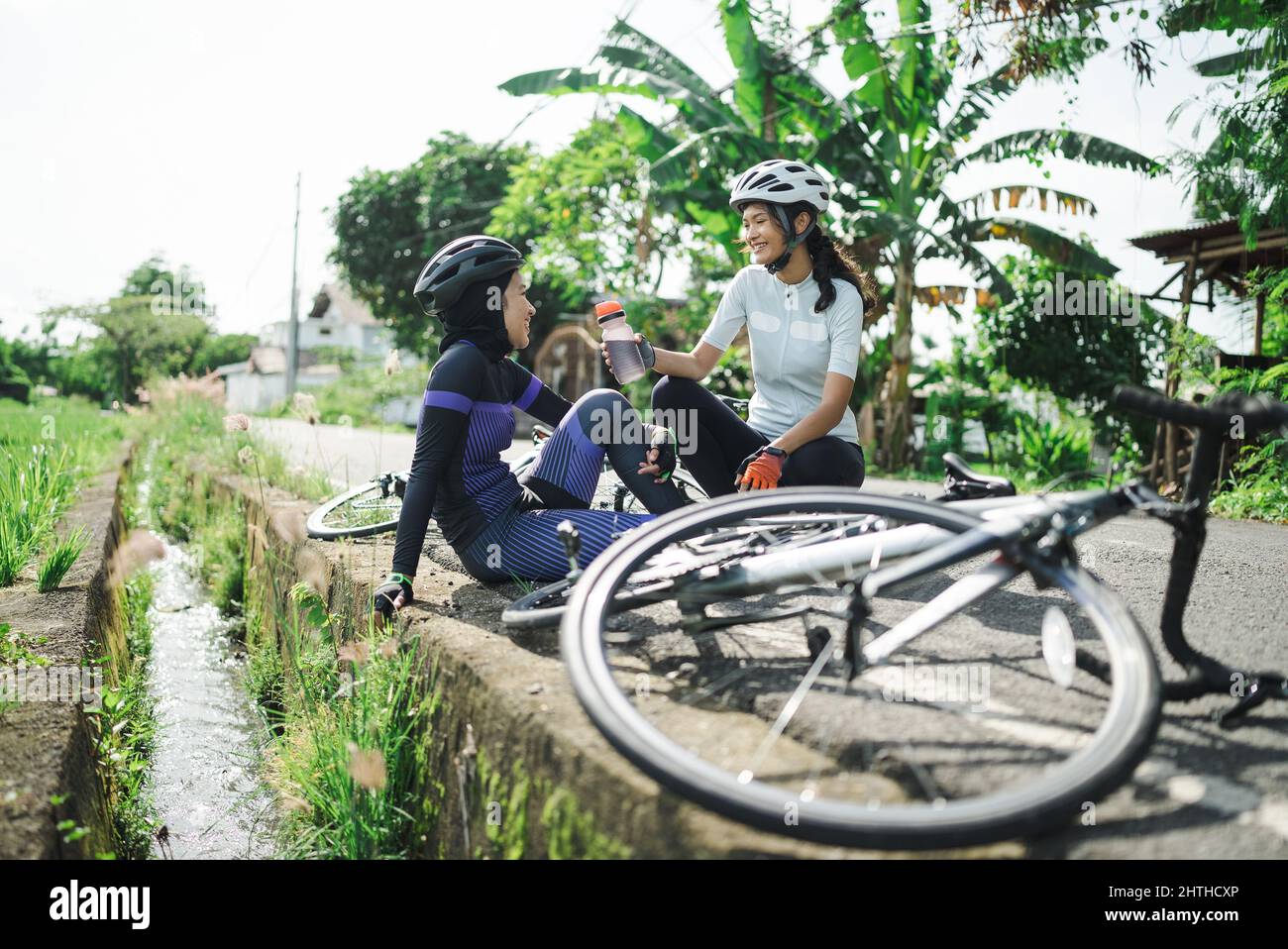 woman cyclist giving a bottle of water to her friend's Stock Photo - Alamy