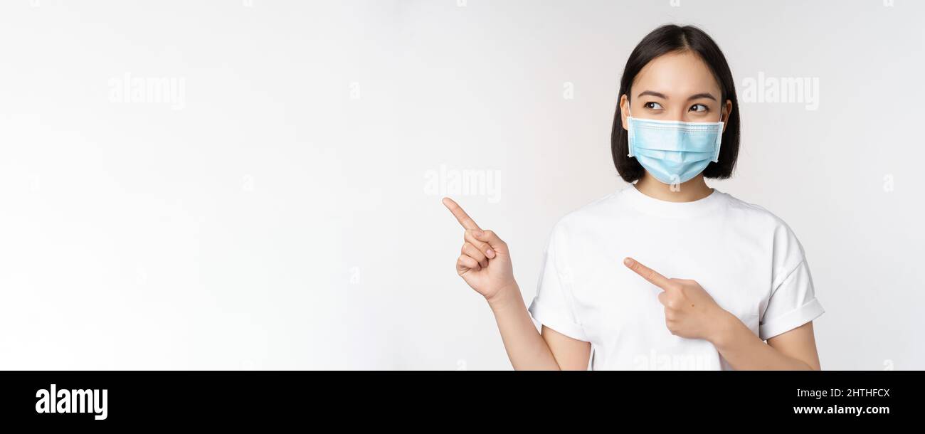 Young korean woman in medical face mask pointing fingers left and ...