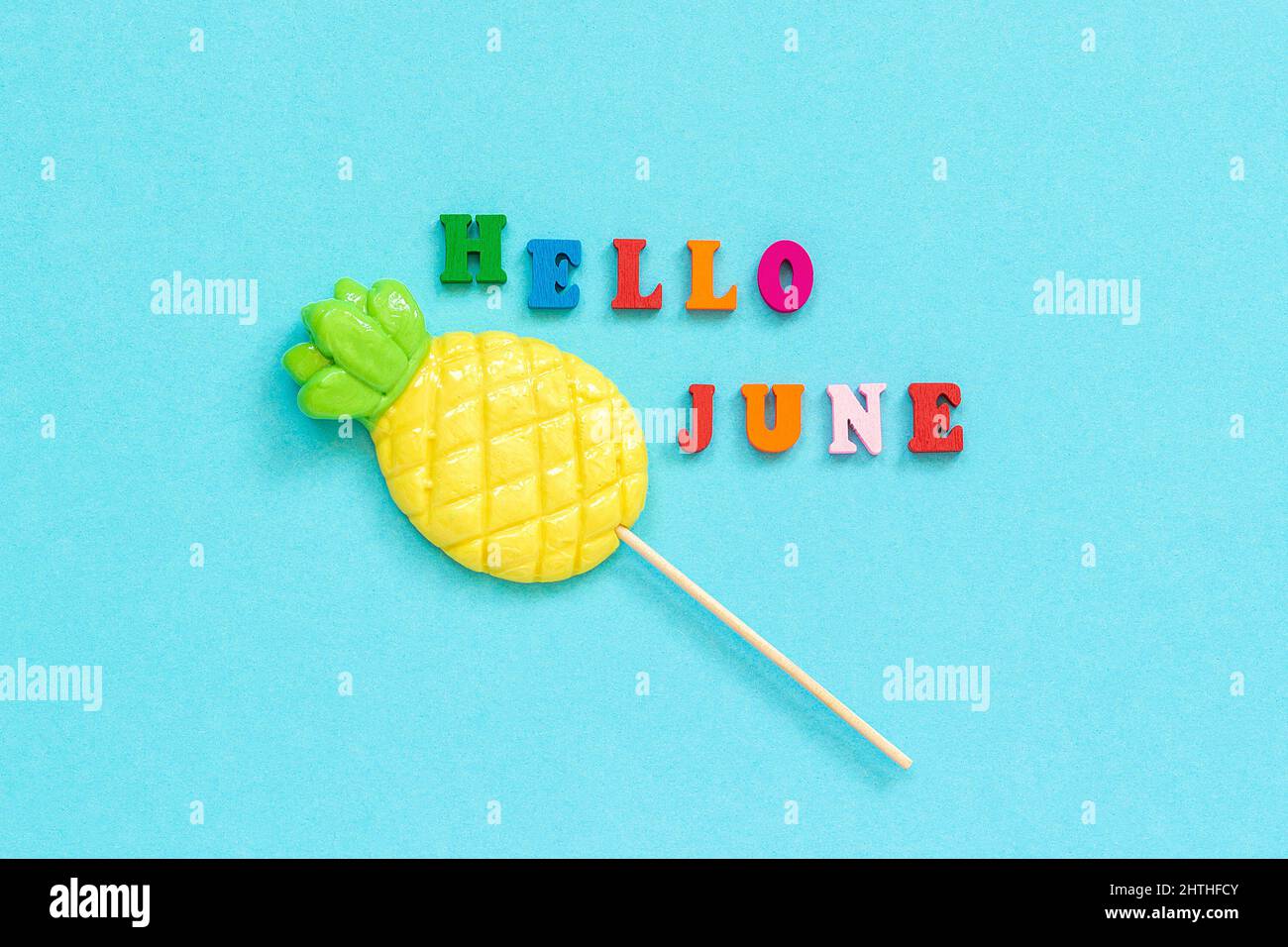 Hello June colorful text, pineapple lollipop on stick on blue paper ...