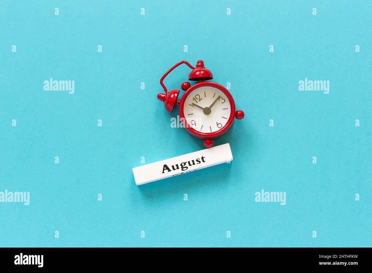 Wooden calendar summer month August and red alarm clock on blue paper ...