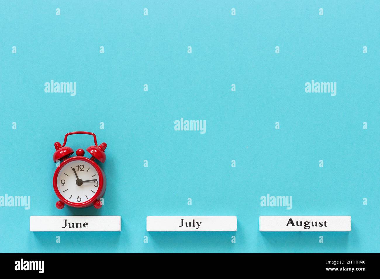 Wooden calendar summer months and red alarm clock over June on blue ...