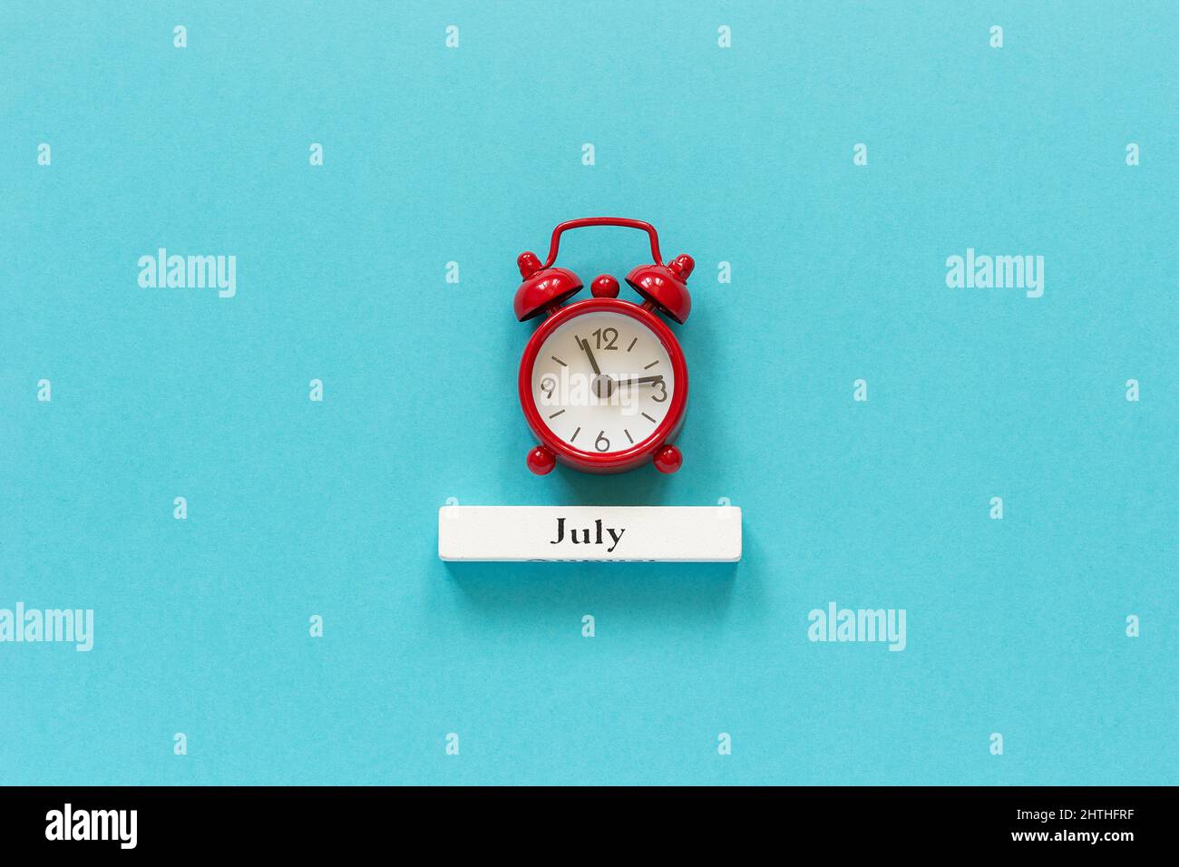 Wooden calendar summer month July and red alarm clock on blue paper ...