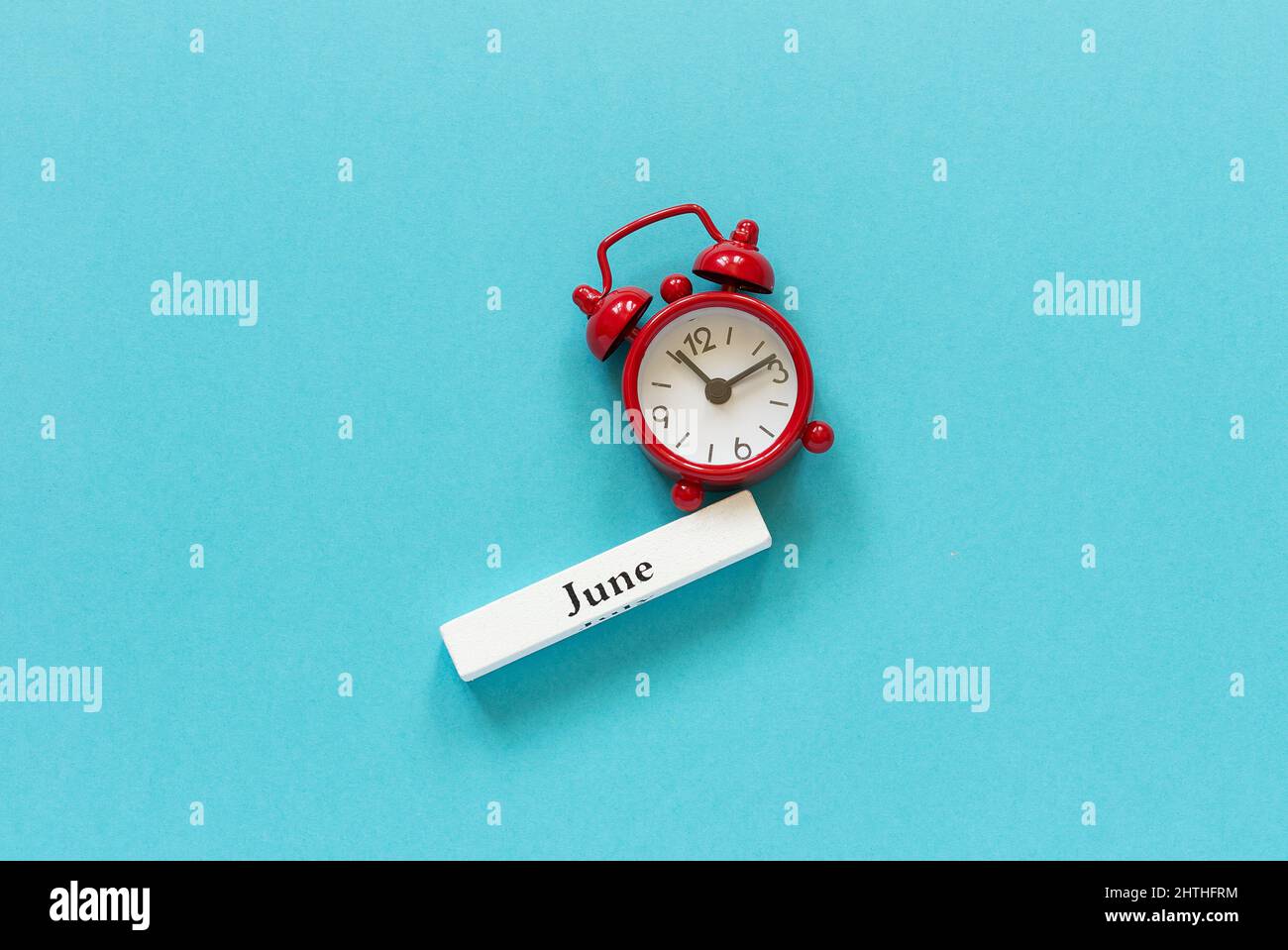 Wooden calendar summer month June and red alarm clock on blue paper ...