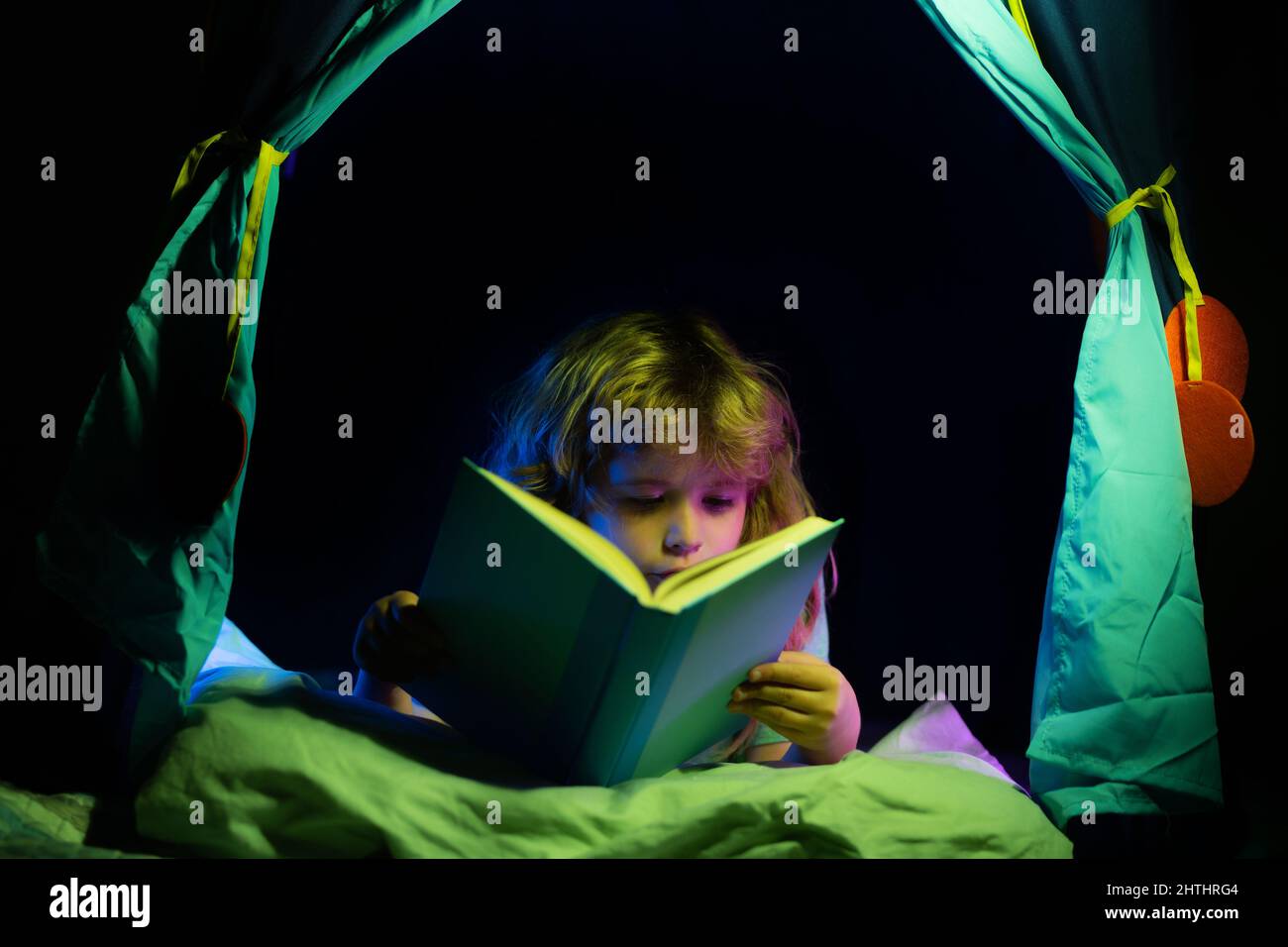 Kids in kids tent reading a book in the dark home. Child boy reading a ...
