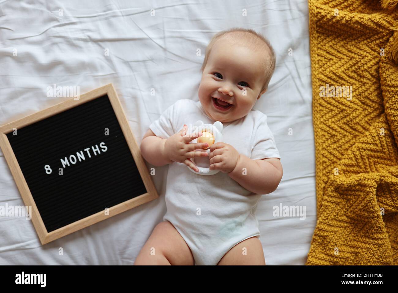 Caucasian blonde baby eight months old lying on cozy bed with yellow ...