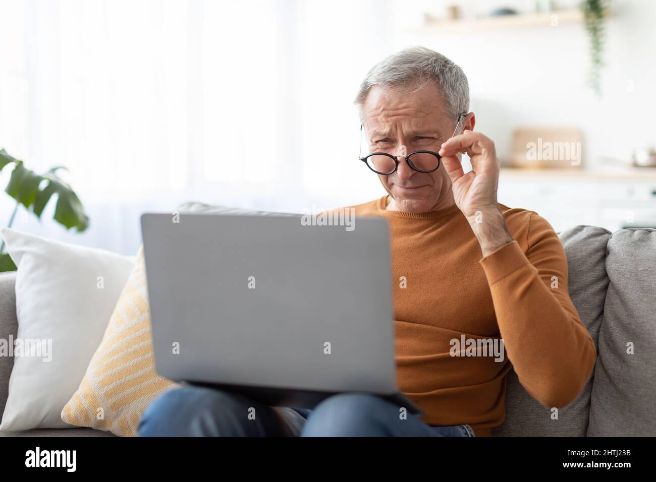 Mature man squinting using laptop, looking at screen Stock Photo - Alamy