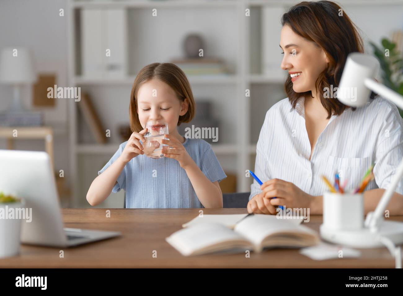 Happy child and adult are sitting at desk. Girl doing homework or ...
