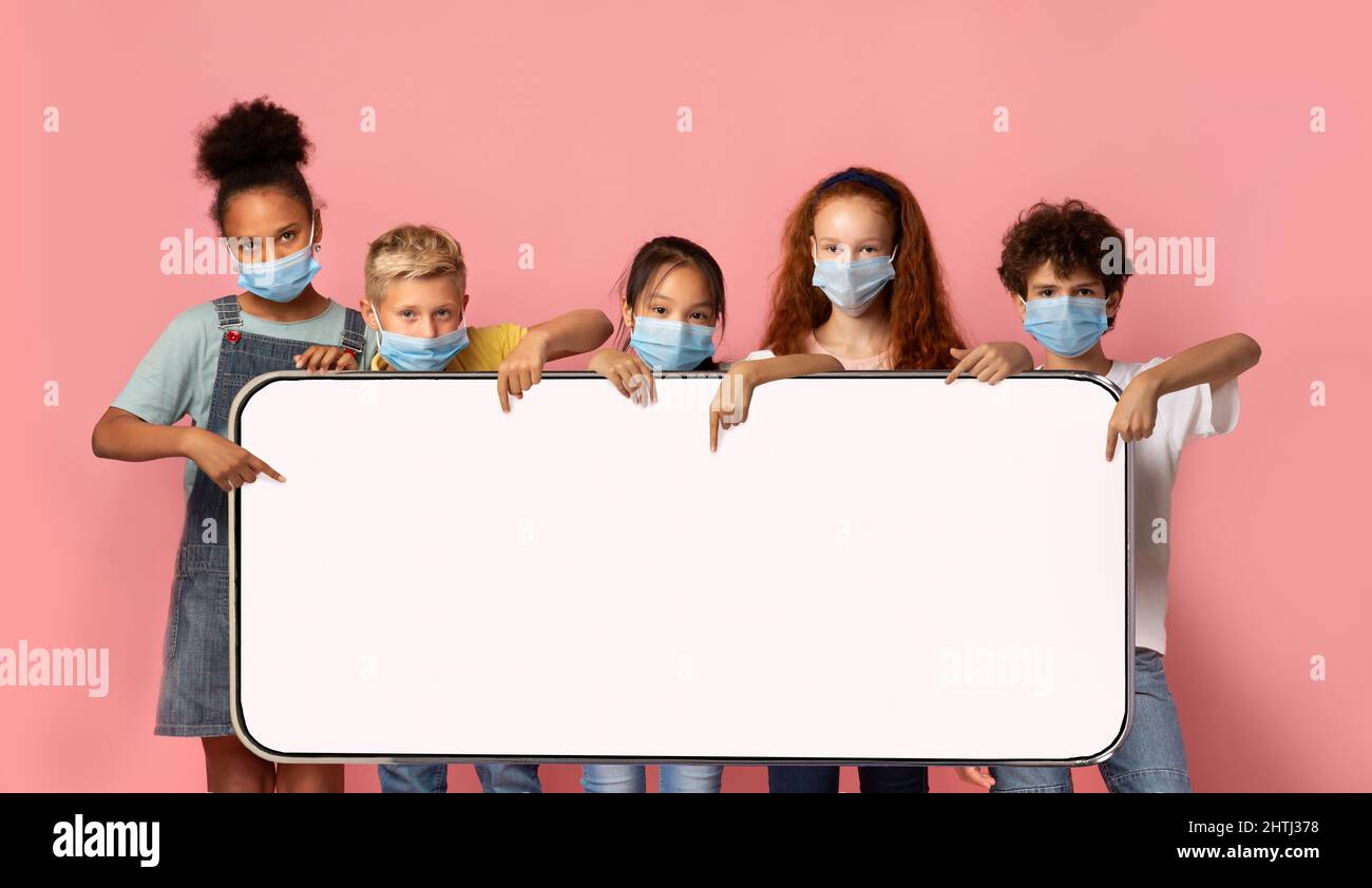 Group of multiethnic kids wearing medical masks holding big blank ...