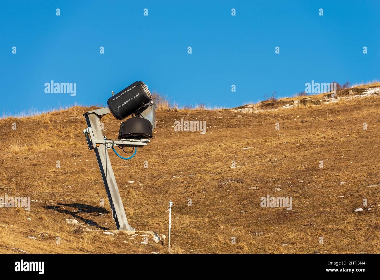Snow cannon or snowmaking system in winter on a brown meadow, ski slope ...