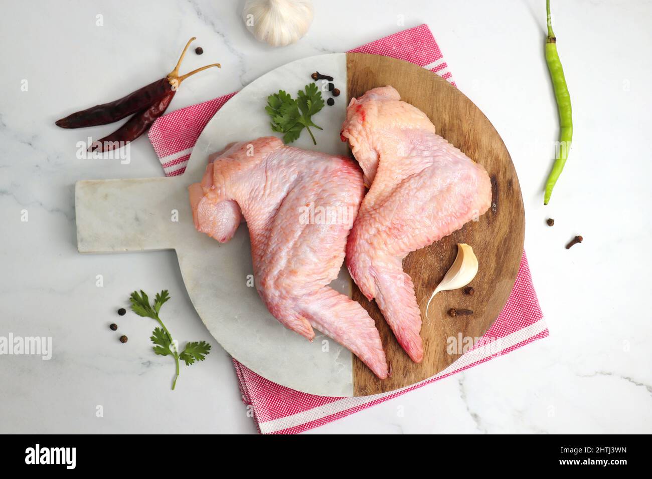 Raw chicken wings on a black plate along with spices such as black ...