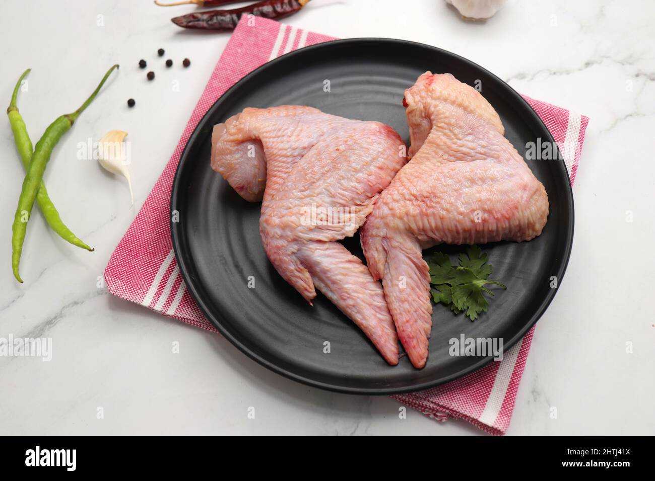 Raw chicken wings on a black plate along with spices such as black ...