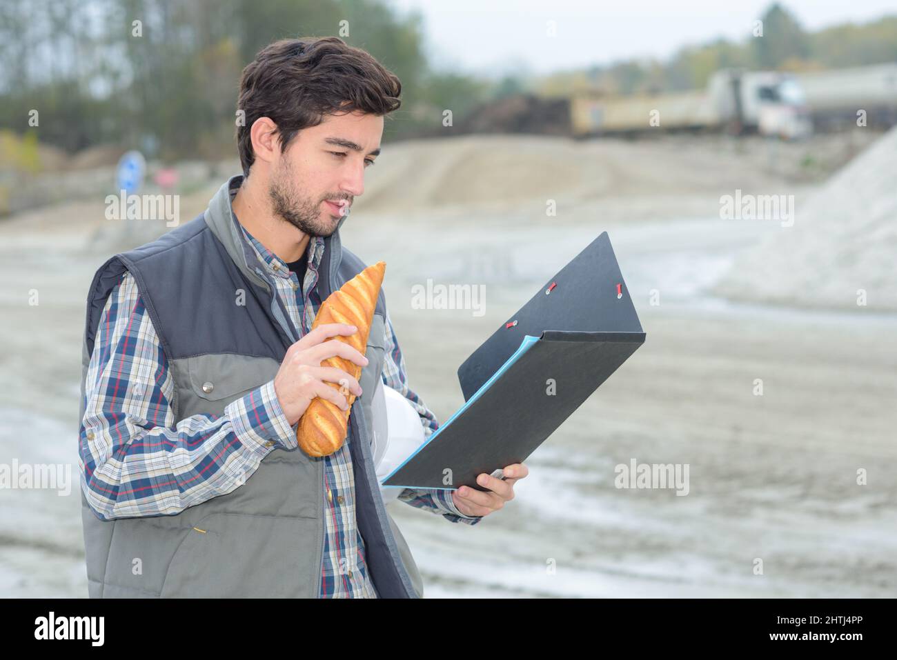 Man eating baguette and looking at file on construction site Stock ...