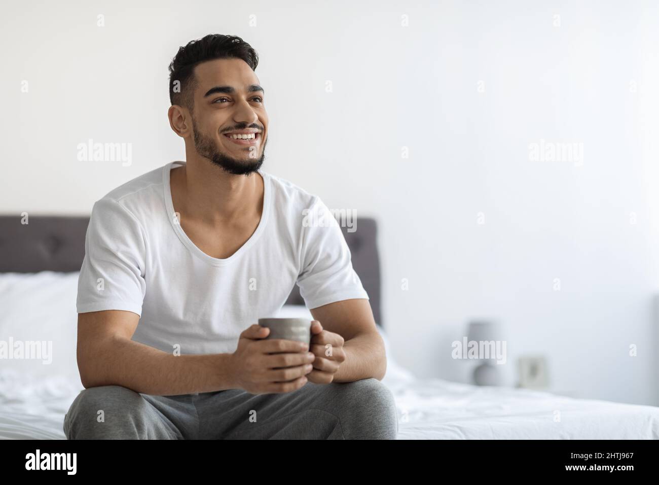 Happy Young Arab Man Relaxing On Bed With Cup Of Coffee Stock Photo - Alamy