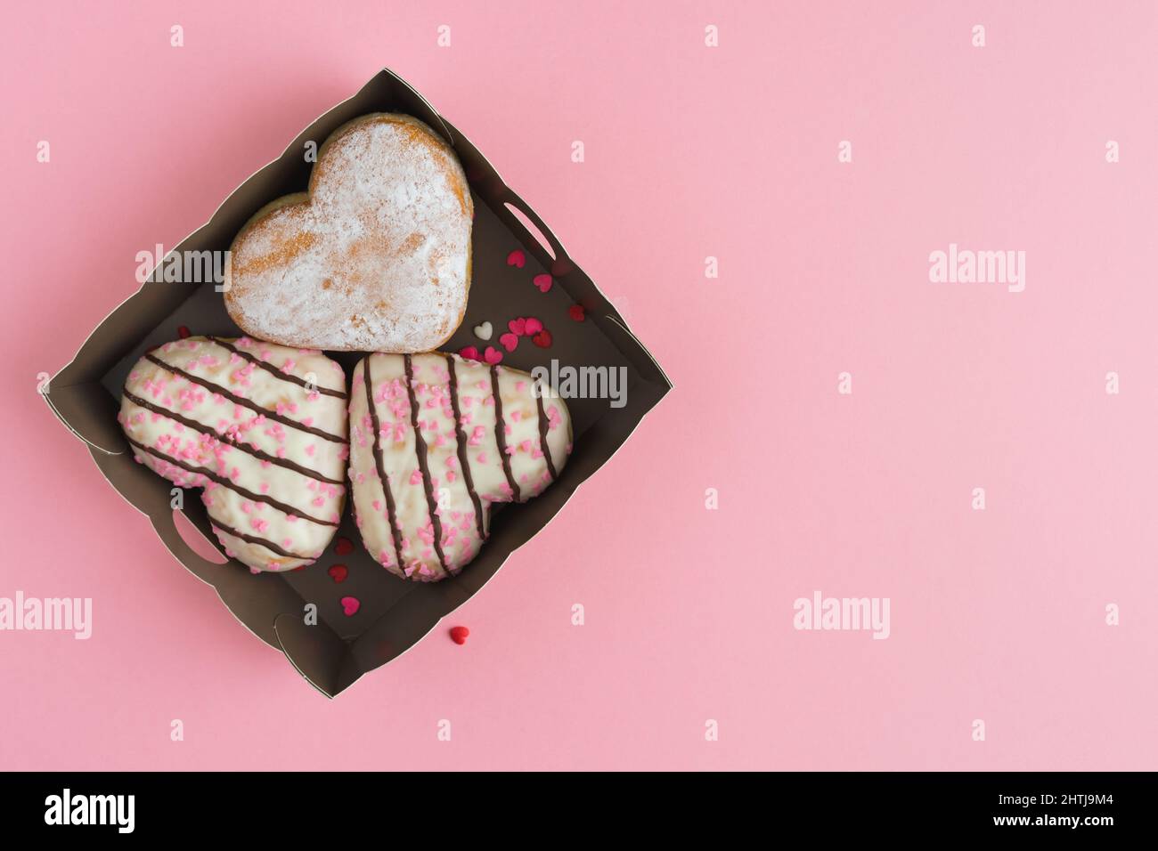 Three heart shaped Donuts inside a box on a pink background. Copy space ...