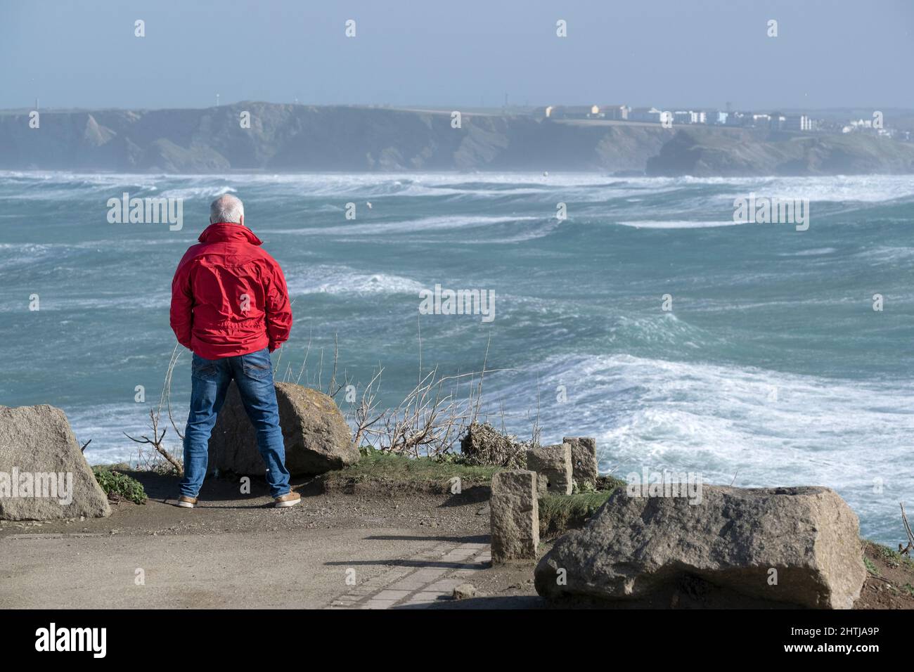 A man in a bright red jacket standing braced against the storm force ...