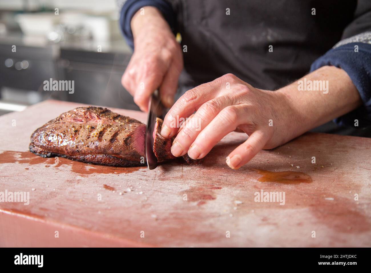 Crop unrecognizable male cook in uniform cutting medium rare beef steak ...