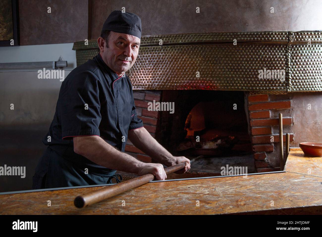 Side view of male chef in uniform putting raw meat into furnace with ...