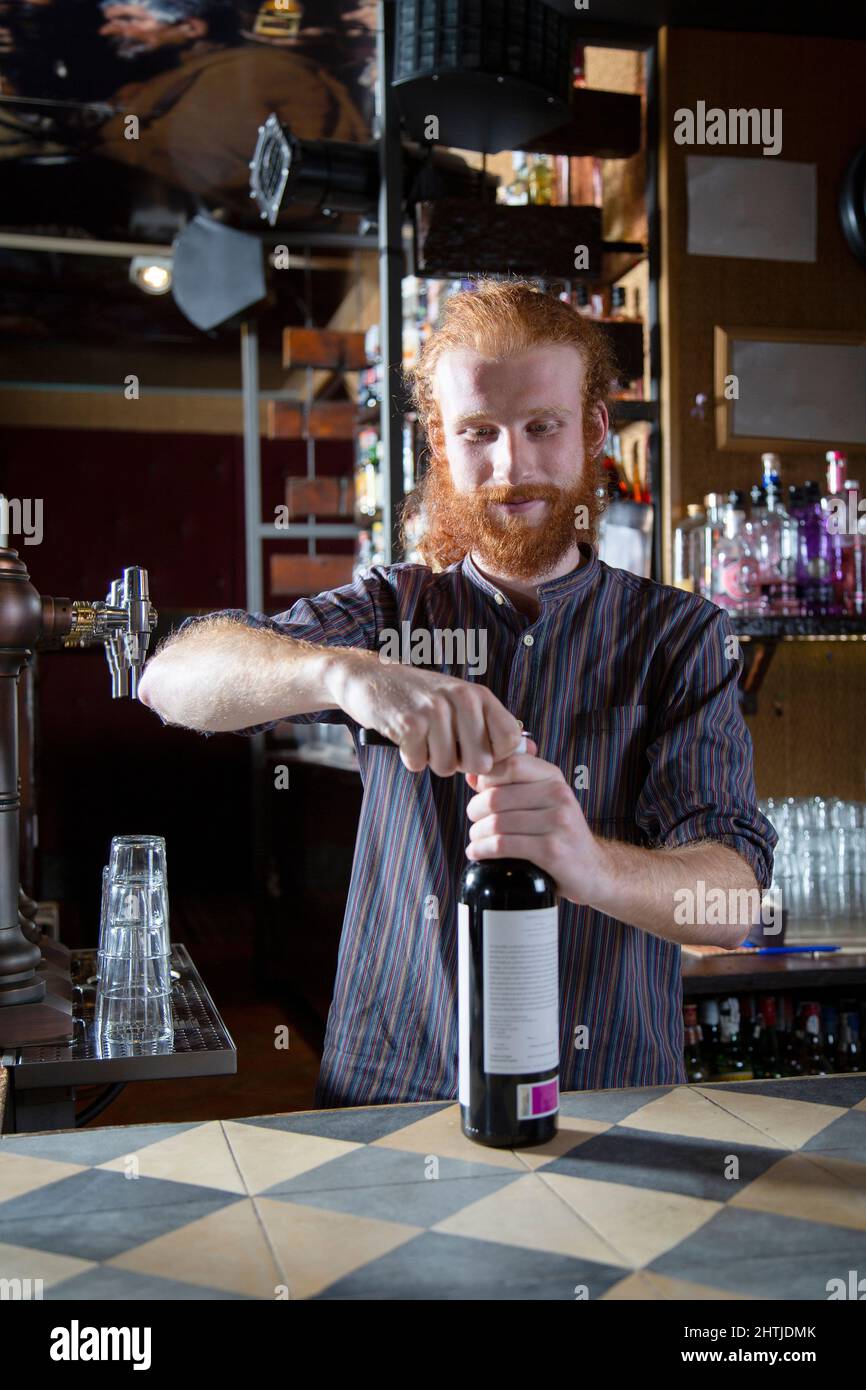 Content male barkeeper with red hair and beard opening bottle of wine ...