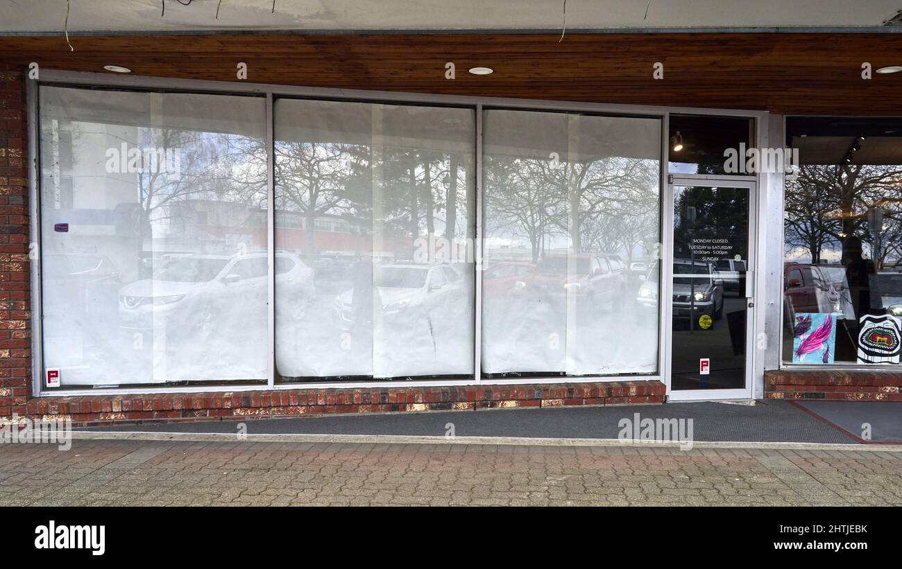 An empty storefront window covered in paper with reflections of parked ...