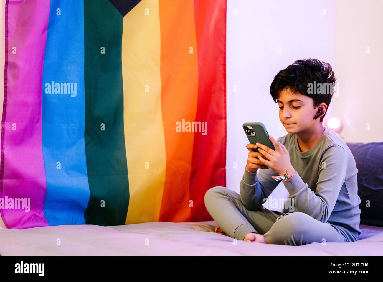 Full body side view of barefoot ethnic boy in wireless earbuds sitting ...