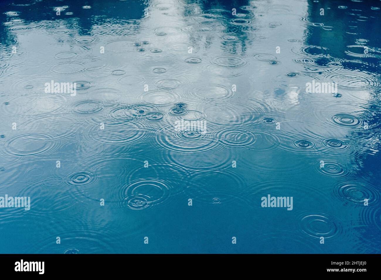 Full frame drops of rain rain dripping on clear rippled water surface ...