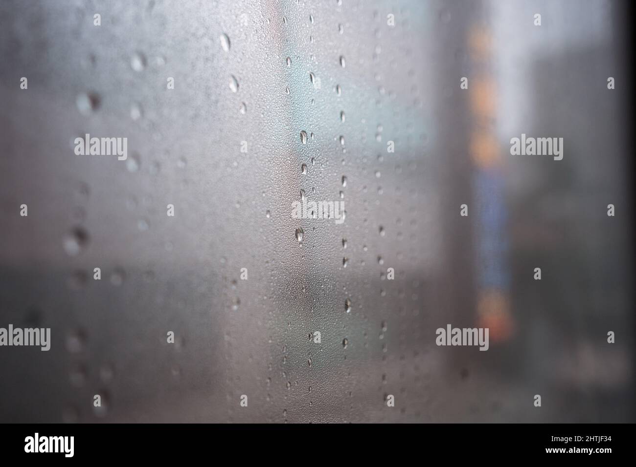 Misted glass window with raindrops in light room overlooking blurred ...