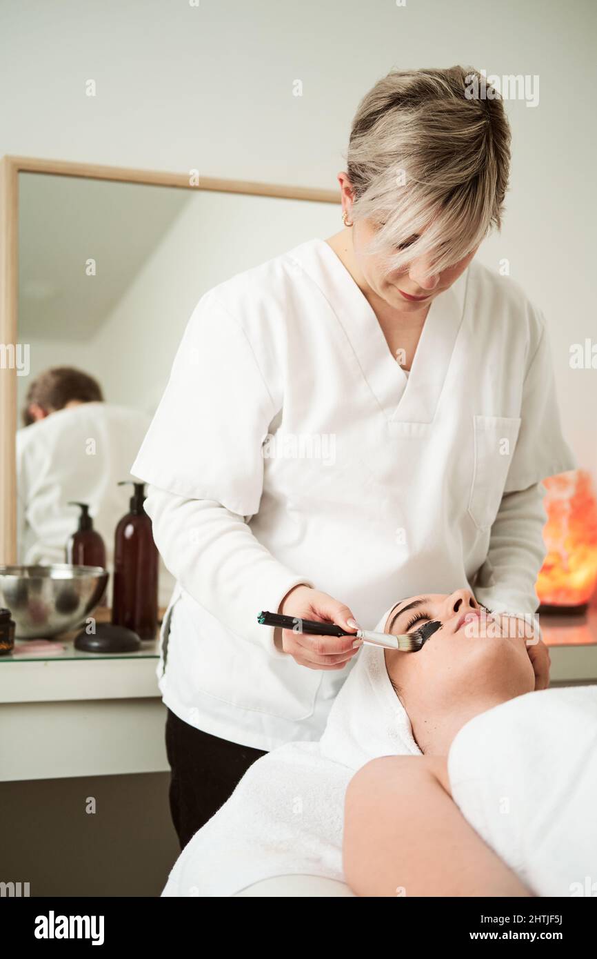 Professional cosmetician applying black anti aging mask on face of ...