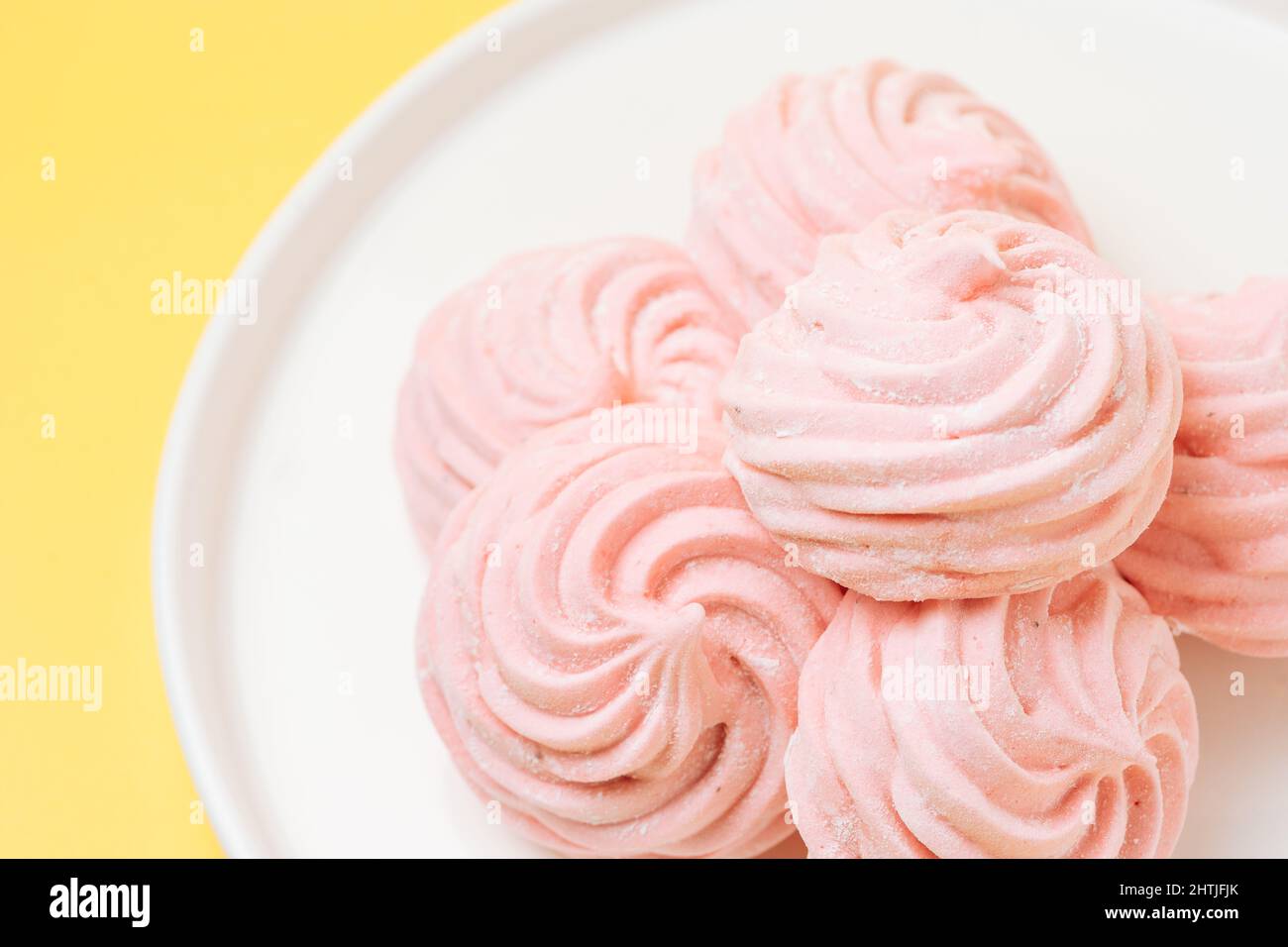 Pile of fresh tasty pink zefir with ridged textured surface served on white plate in light room ...