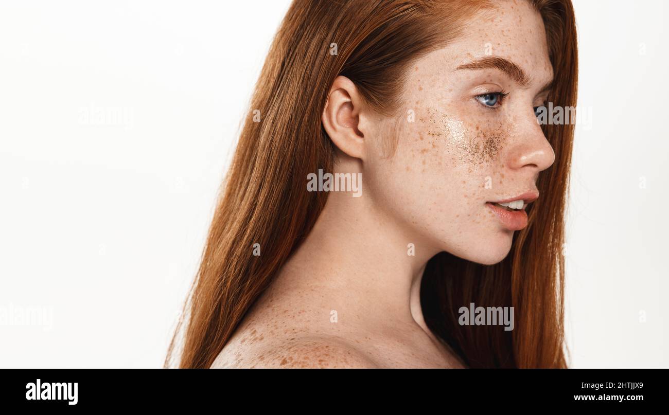 Profile portrait of redhead woman with glitter under eyes, glowing healthy pale skin and ...
