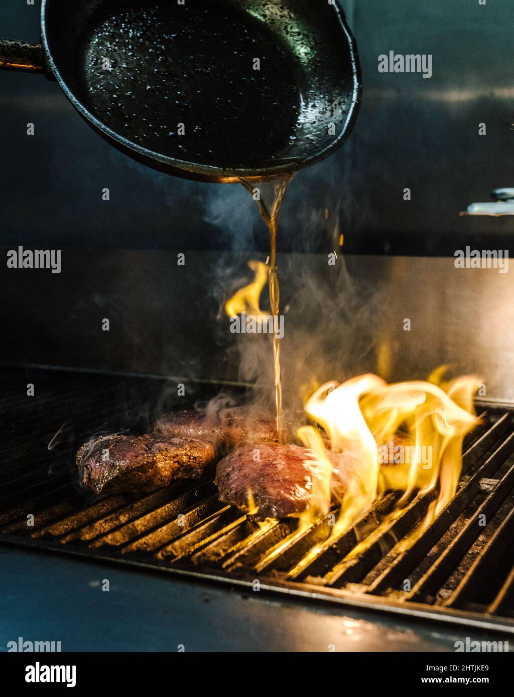 Vertical shot of a pan pouring oil on a grill with burning flames and ...