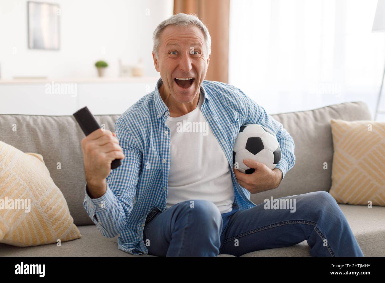 Excited mature man watching tv celebrating goal holding ball Stock ...