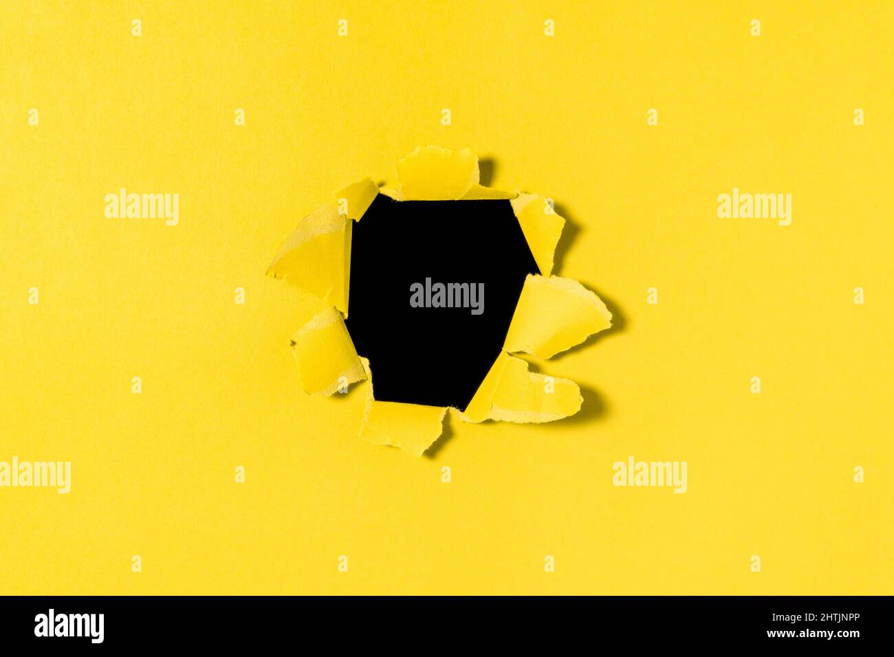 A hole in yellow paper with torn edges and a black background inside ...