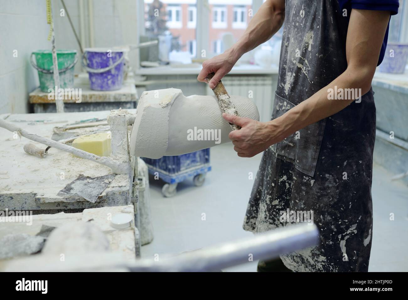 Young worker of prosthetic factory polishing workpiece with chisel while standing in front of ...