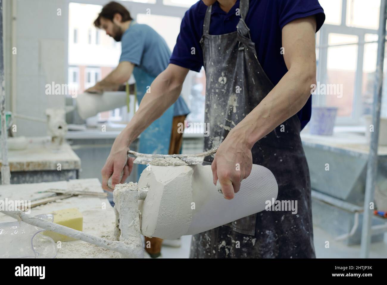 Young worker in apron holding worktool while grinding plaster cast of ...