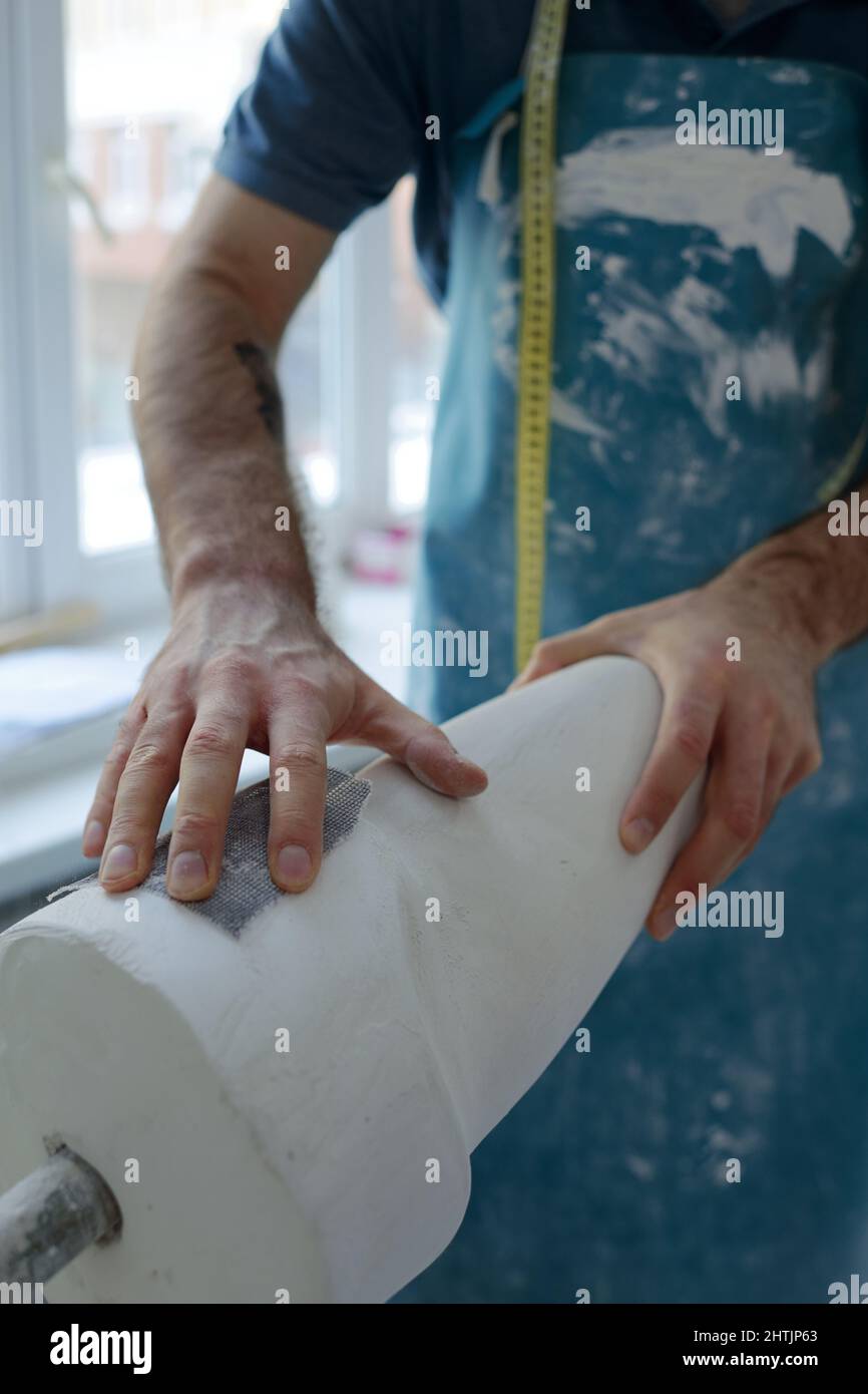 Hand of male specialist in apron rubbing surface of plaster workpiece ...