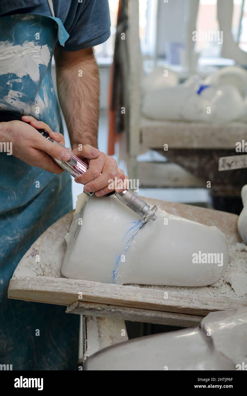 Hands of young manufactory worker in apron cutting part of plaster cast ...