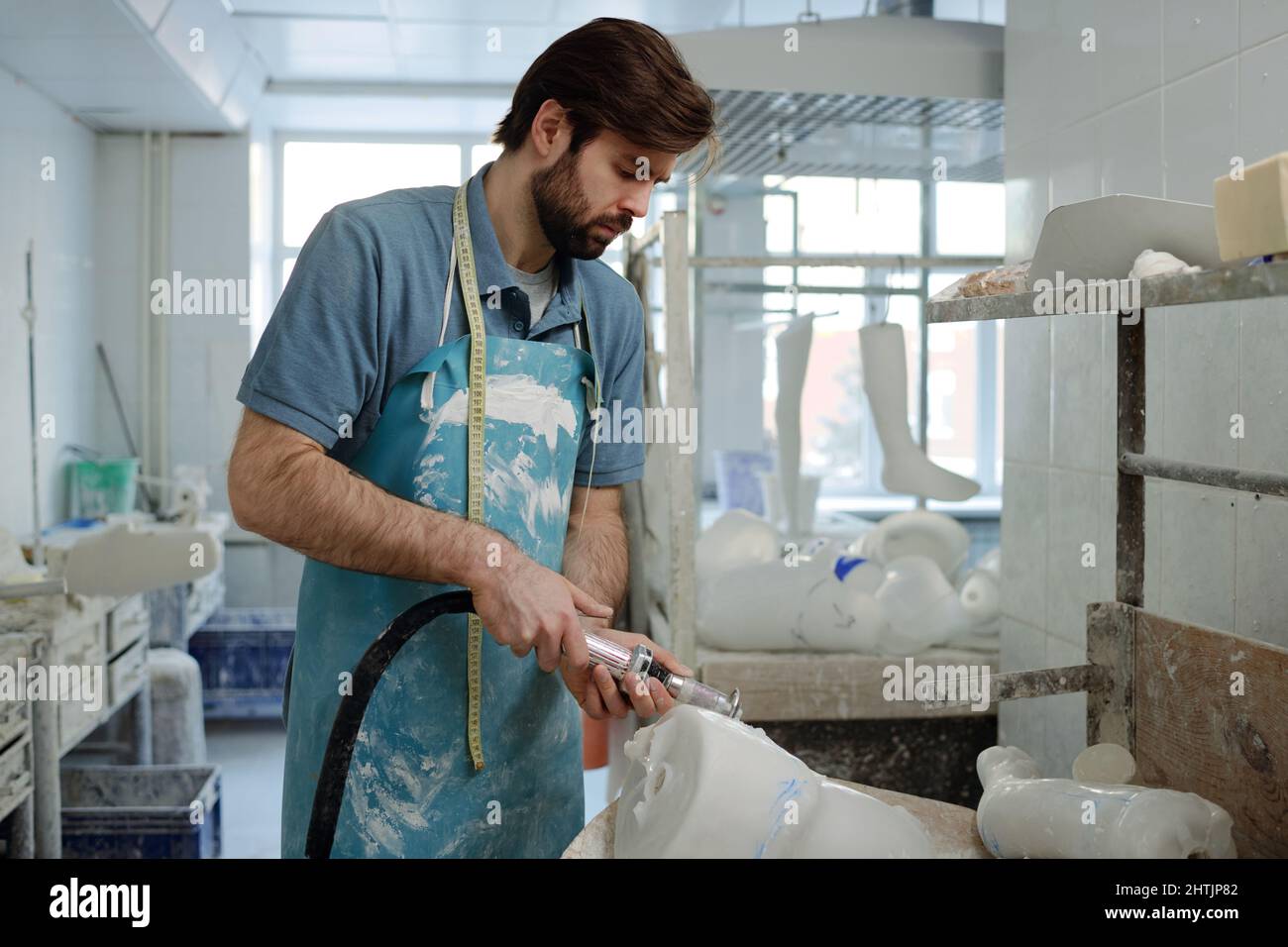 Side view of bearded skilled worker od prosthetic factory with electric worktool cutting upper ...