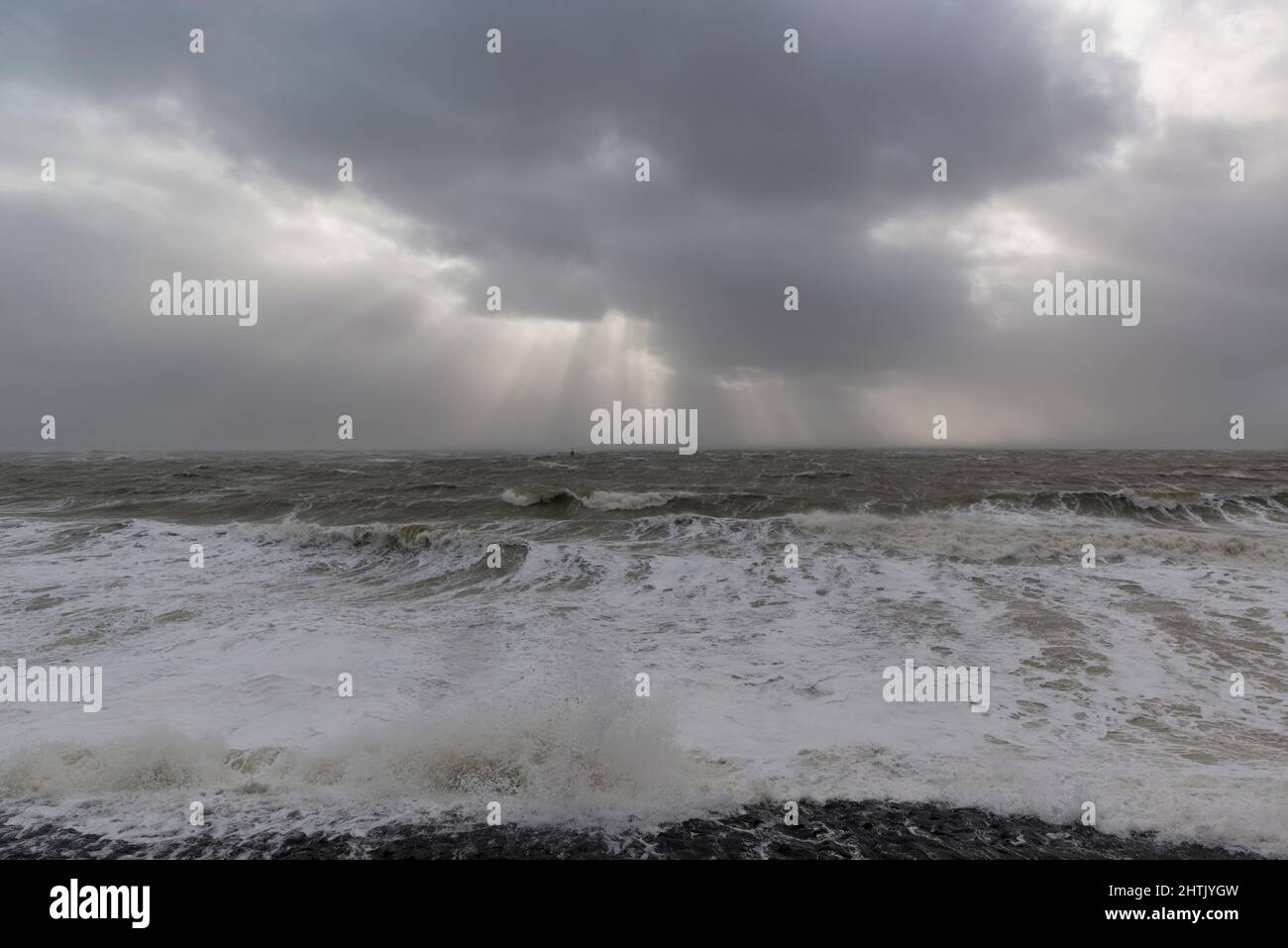 Sun rays from behind the clouds shine on the turbulant waves during the ...