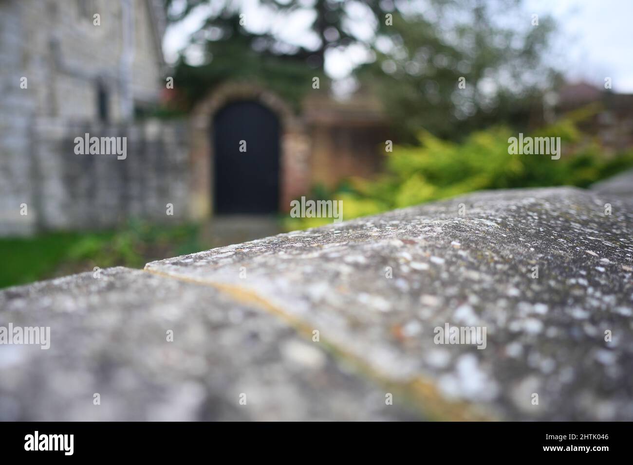 Shallow focus of snowy rocky ground with blurred house with trees ...